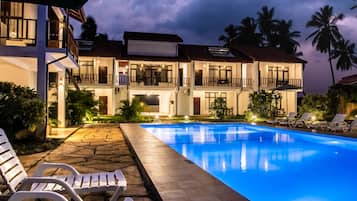 Um hotel com vários andares, piscina, área de estar externa e palmeiras.