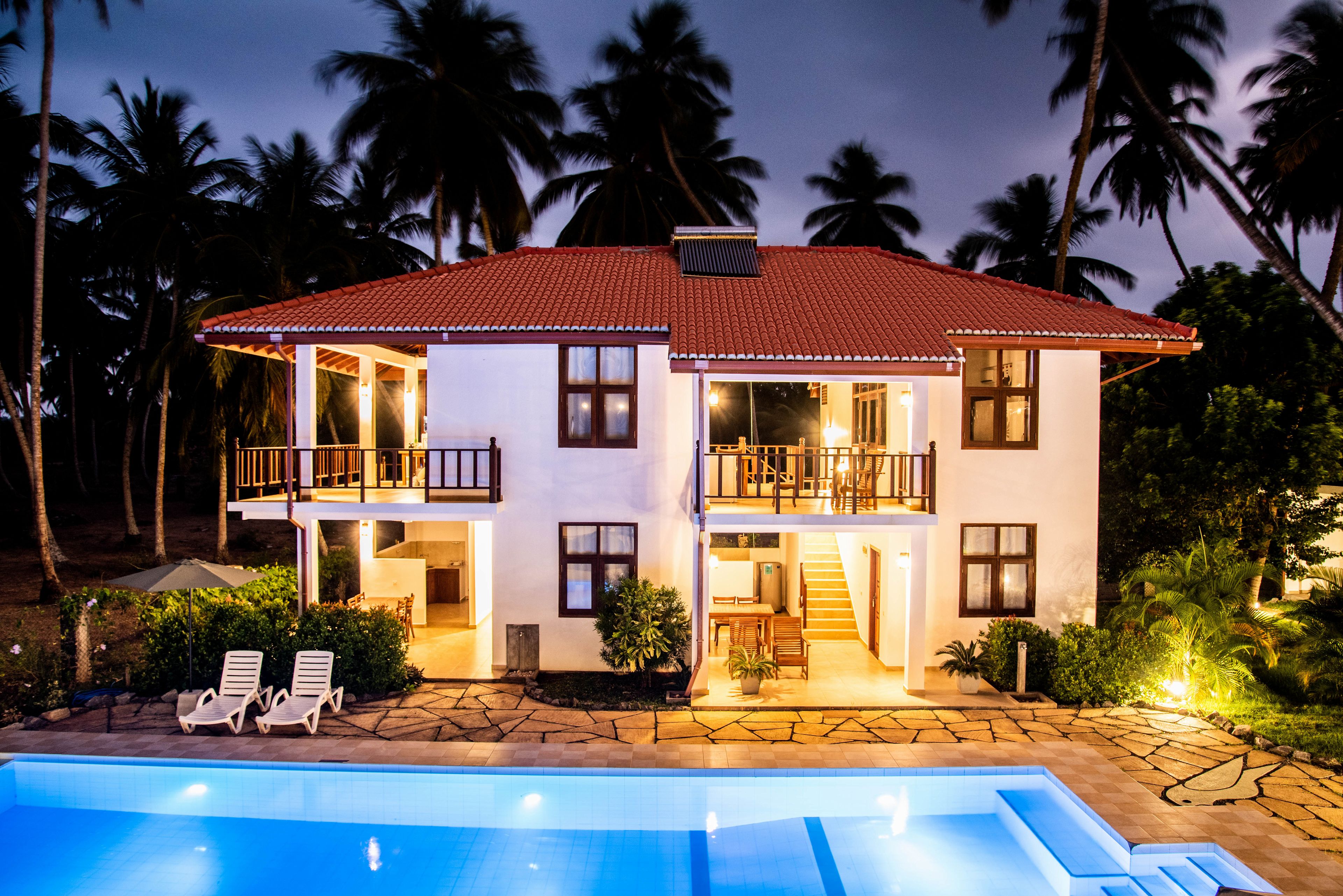 Uma casa de dois andares com piscina, varandas e telhado de telhas vermelhas.