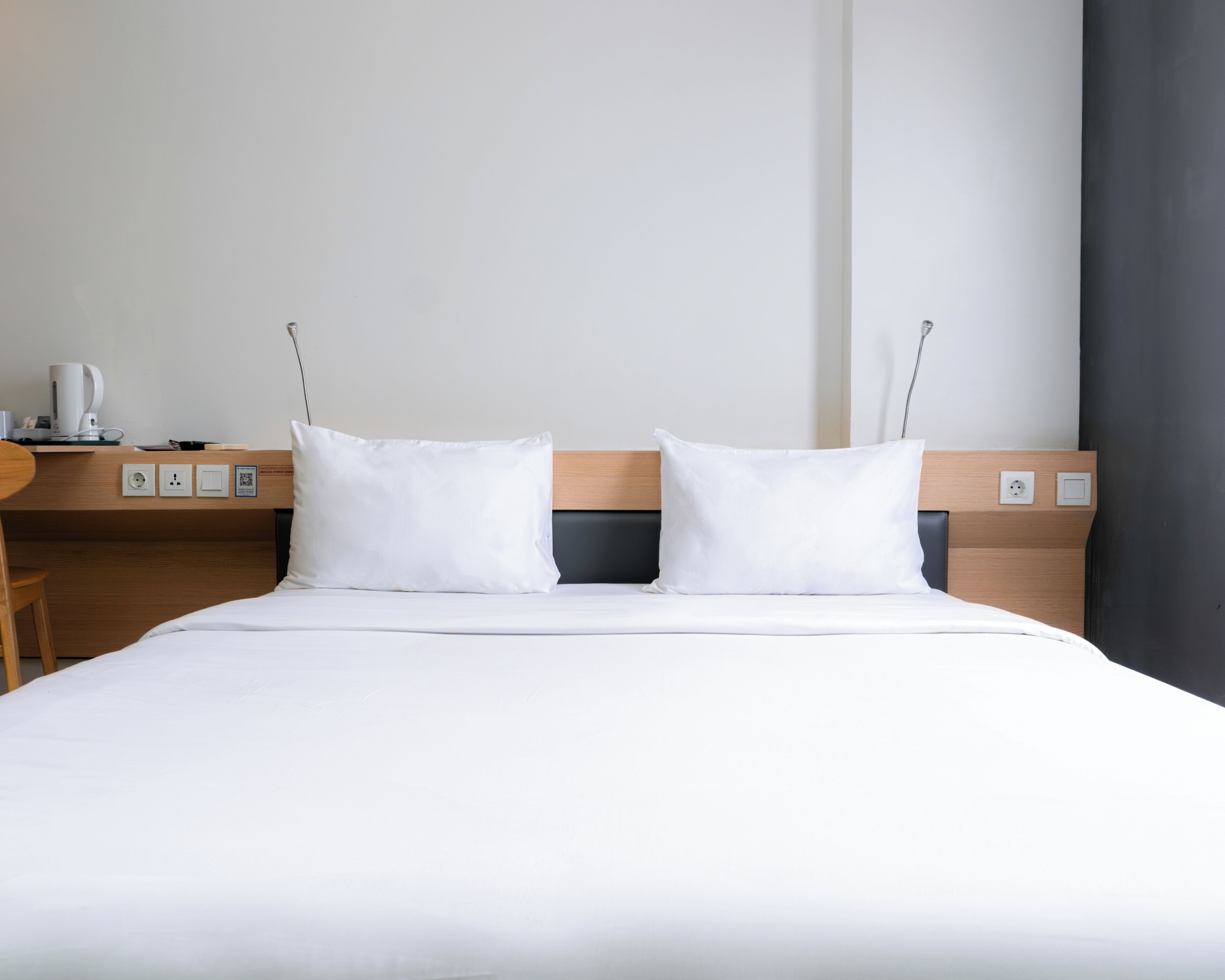 Cama bem arrumada com duas almofadas e cabeceira de madeira.