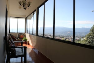 Varanda com vista para um horizonte urbano e montanhas. Há duas cadeiras e um vaso com planta.
