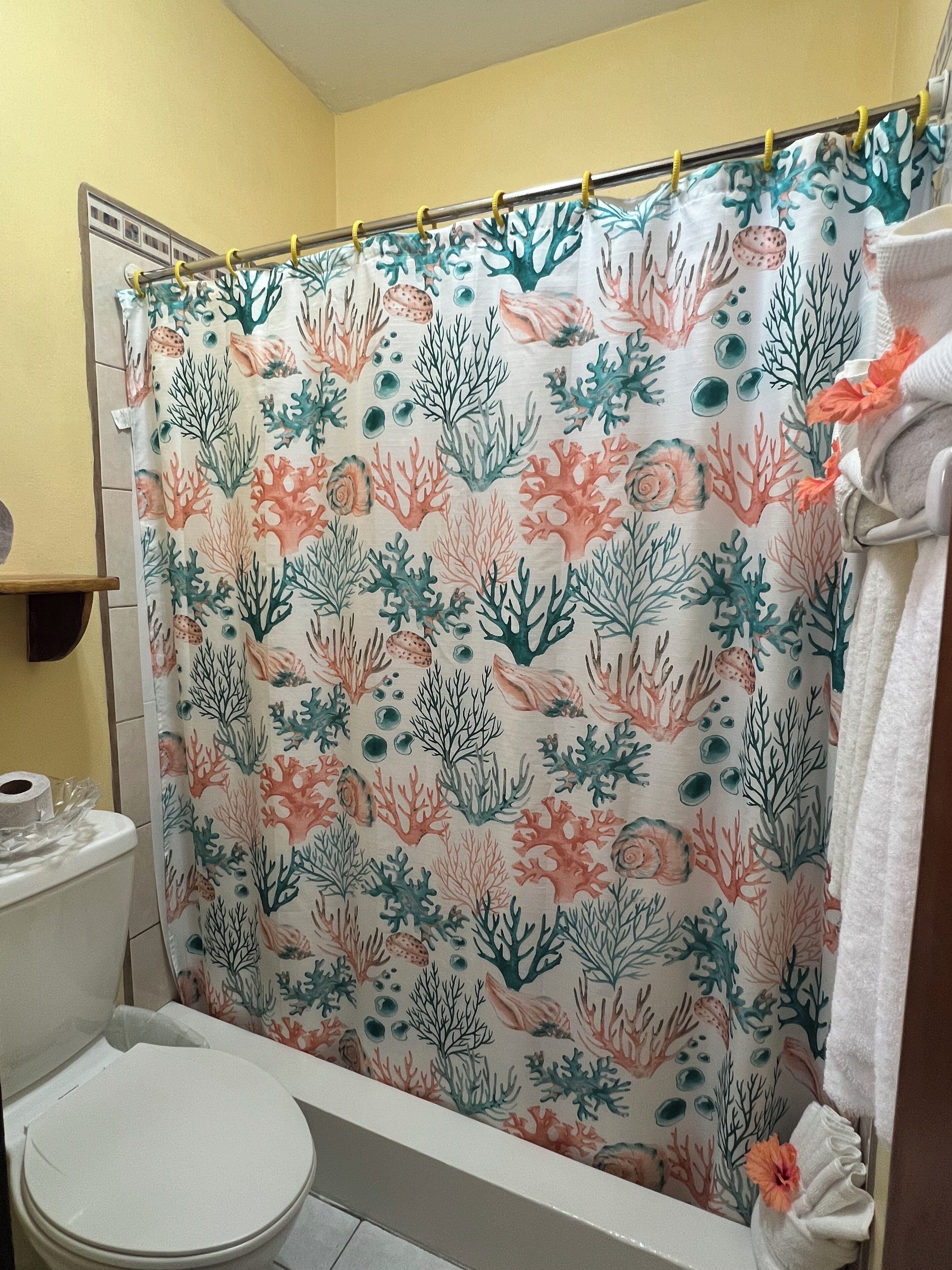 Casa de banho com cortina de chuveiro estampada com um padrão de recife de coral, sanita e suporte para toalhas.