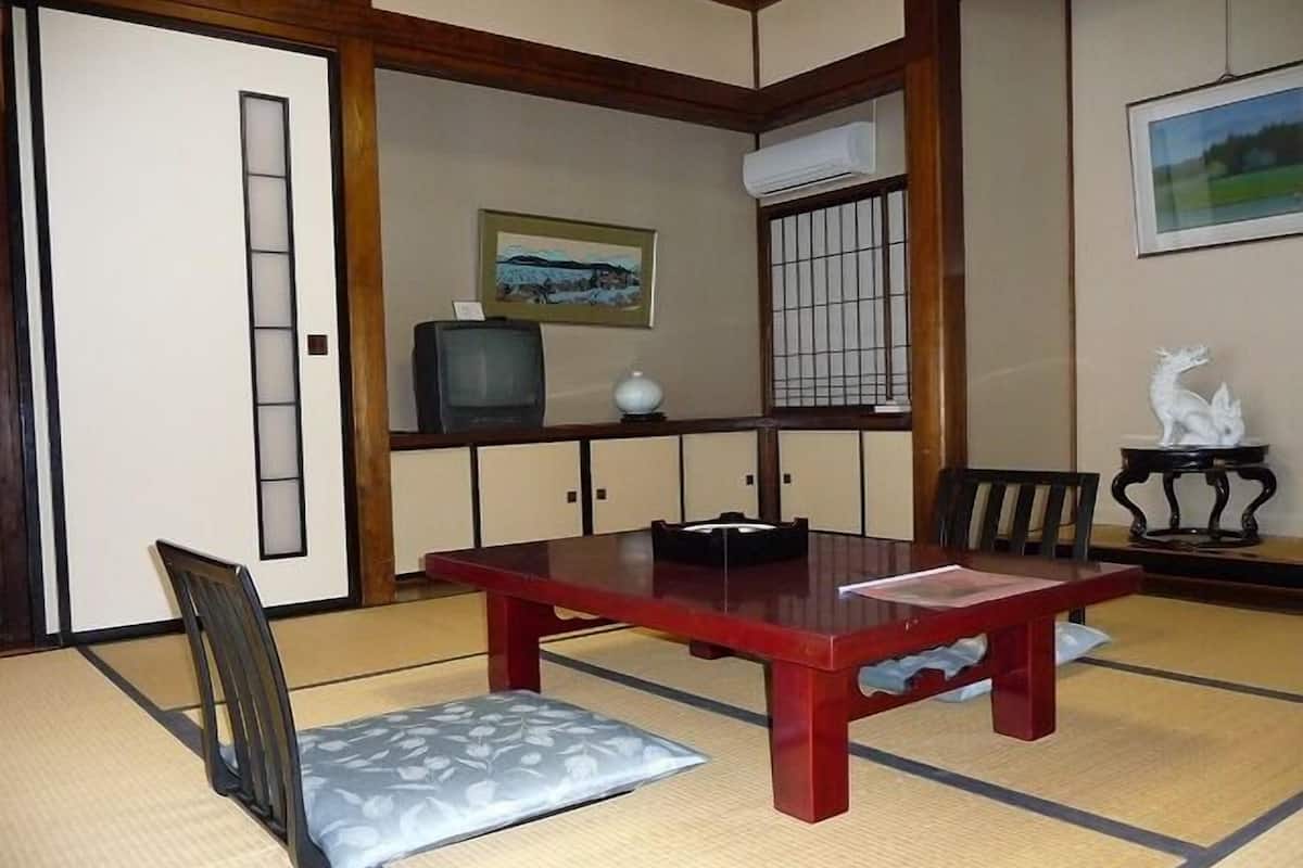 Um espaço com tatames, uma mesa baixa, cadeiras, uma televisão e uma estátua decorativa.
