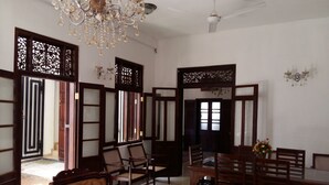 Quarto tradicional com área de jantar, mobiliário de madeira e elementos decorativos como um candelabro e arandelas.