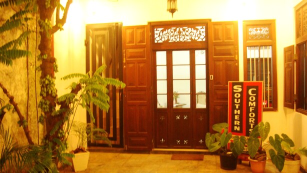 Uma porta de madeira com painéis de vidro, um letreiro com a inscrição "Southern Comfort" e plantas em vasos na frente.