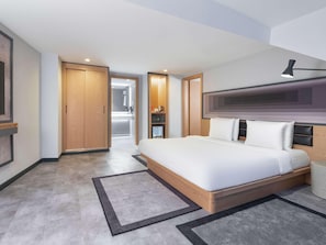 Quarto de hotel moderno com uma cama grande, cabeceira de madeira, televisão integrada e closet espaçoso.