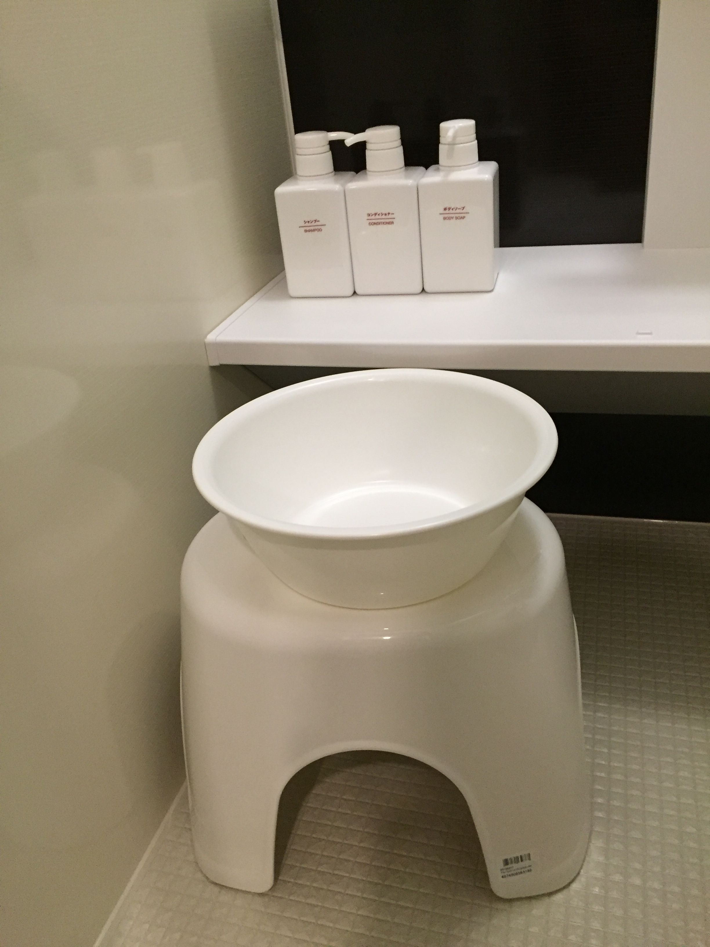 Um banheiro com uma pia de pedestal branca e três frascos de produtos de higiene em uma prateleira branca.