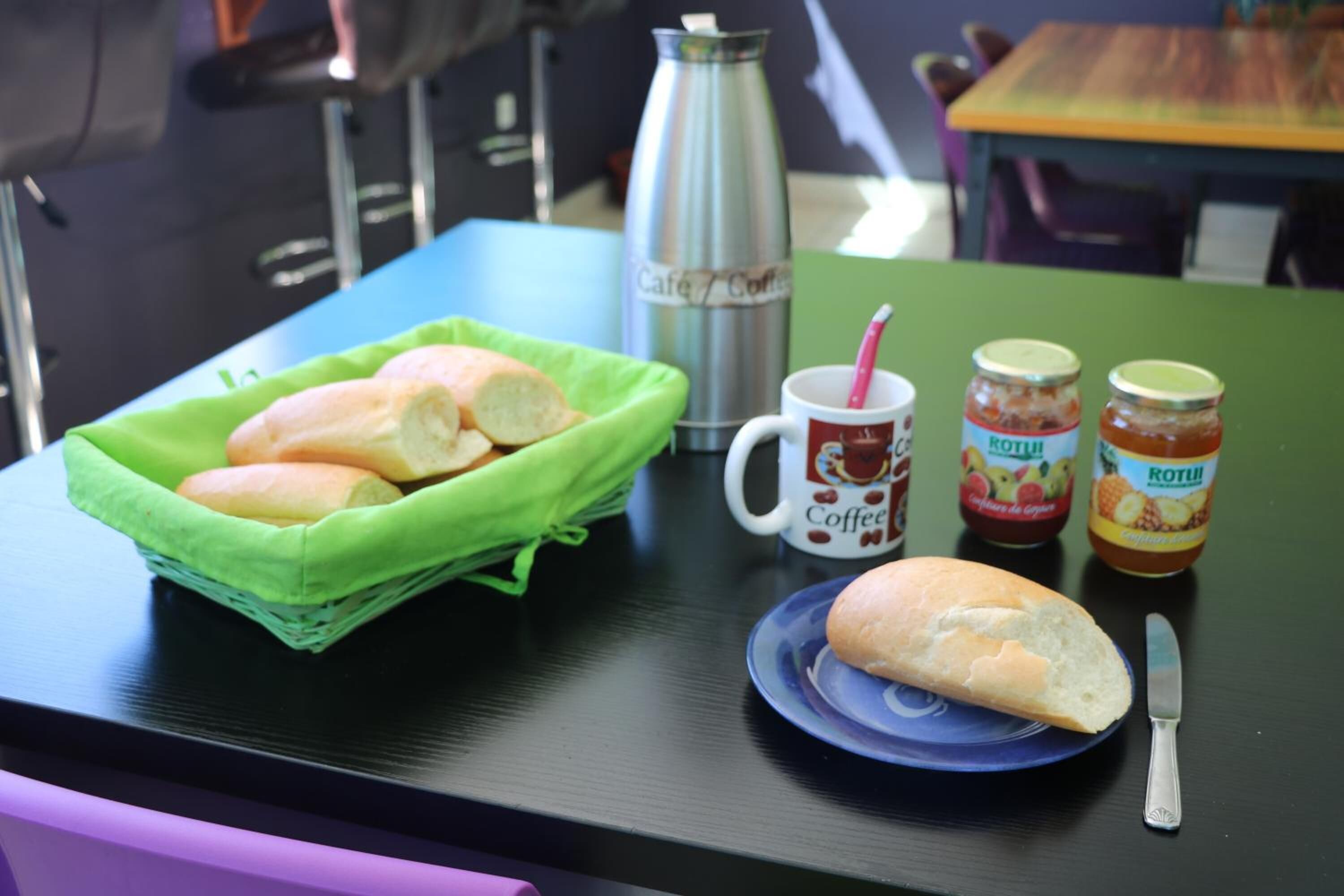 Uma mesa com uma cesta de pão, uma caneca de café e dois potes de geleia.