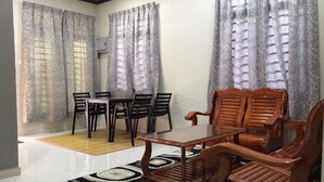 Uma sala de estar com área de refeições, mobiliário de madeira, cortinas estampadas e piso de azulejos.