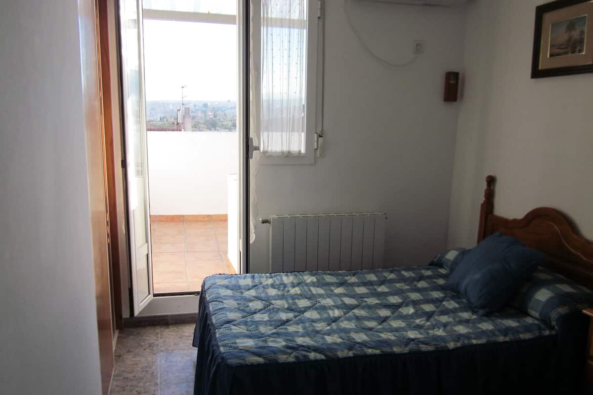 Quarto com cama, radiador, porta que dá para uma varanda e quadro na parede.