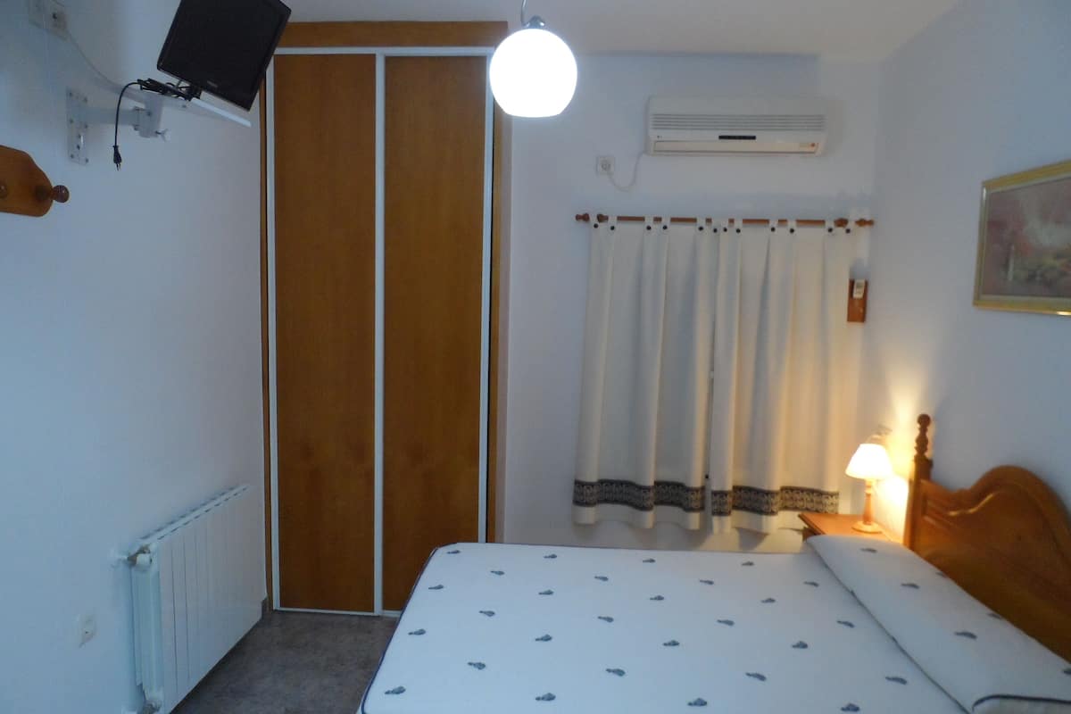 Quarto com cama, mesa de cabeceira com abajur, guarda-roupa, radiador e luz no teto.