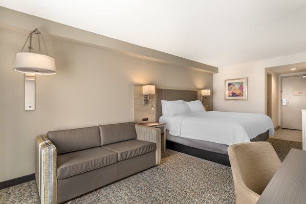 Quarto de hotel com uma cama, um sofá, uma escrivaninha e uma luminária.