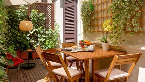 Um deck de madeira com mesa e cadeiras, rodeado por vasos de plantas e um cercado de madeira.