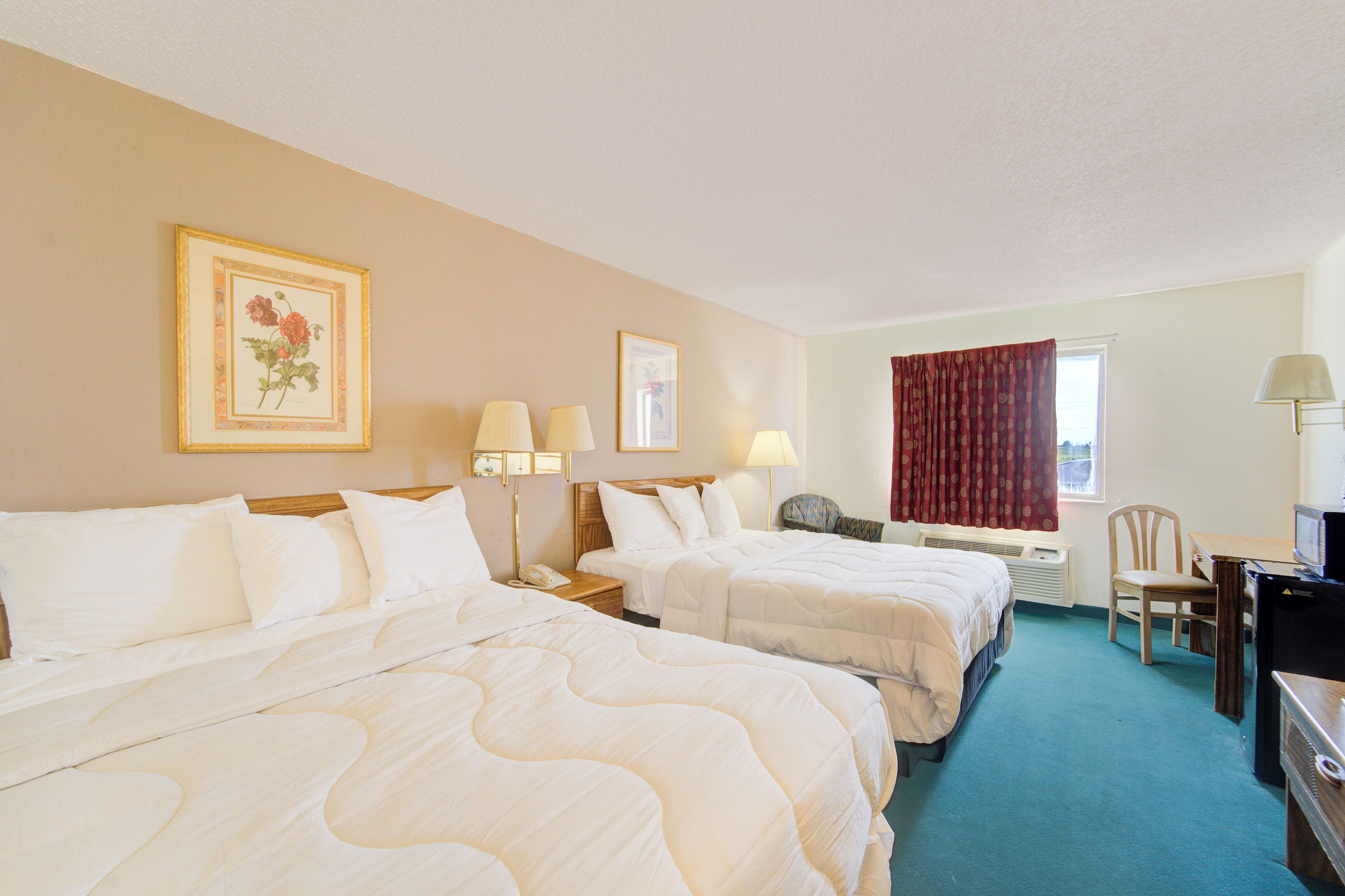 Quarto de hotel com duas camas, uma escrivaninha com cadeira, televisão e janela com cortinas.