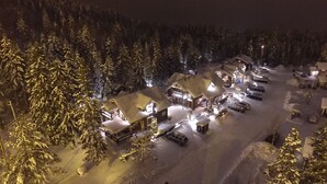 Vila coberta de neve, com várias casas e carros estacionados.