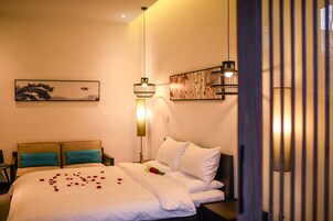 Cama bem arrumada com lençóis brancos e almofadas verde-água, uma obra de arte emoldurada acima dela e uma mesa de cabeceira com abajur.