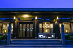 Entrada de hotel com estilo arquitetônico tradicional, apresentando uma placa com caracteres chineses, uma moderna placa iluminada e uma escadaria que leva à entrada.