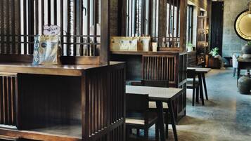 Interior de restaurante com mobiliário de madeira, teto estampado e um grande vaso decorativo.