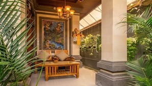 Um banco de madeira com almofadas, um mural e plantas penduradas em um espaço interior bem iluminado.