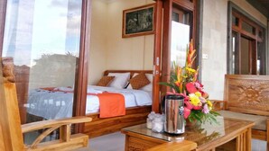 Quarto com cama, mesa com um vaso de flores, cafeteira e uma cadeira.