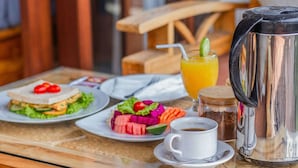 Uma mesa de café da manhã com sanduíche, salada, frutas, café e jarra.