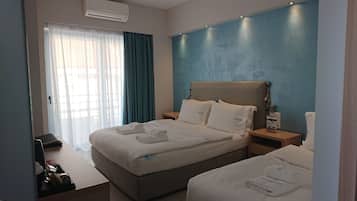 Quarto de hotel com uma cama grande, uma cama menor, uma mesinha de cabeceira com abajur e uma janela com cortinas.