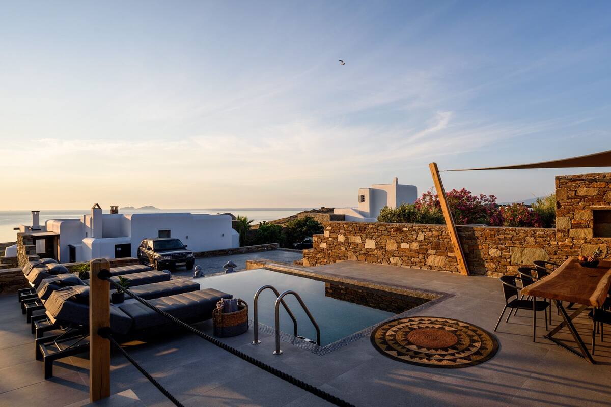 Terraço no telhado com piscina, espreguiçadeiras e área de refeições com vista para o mar.