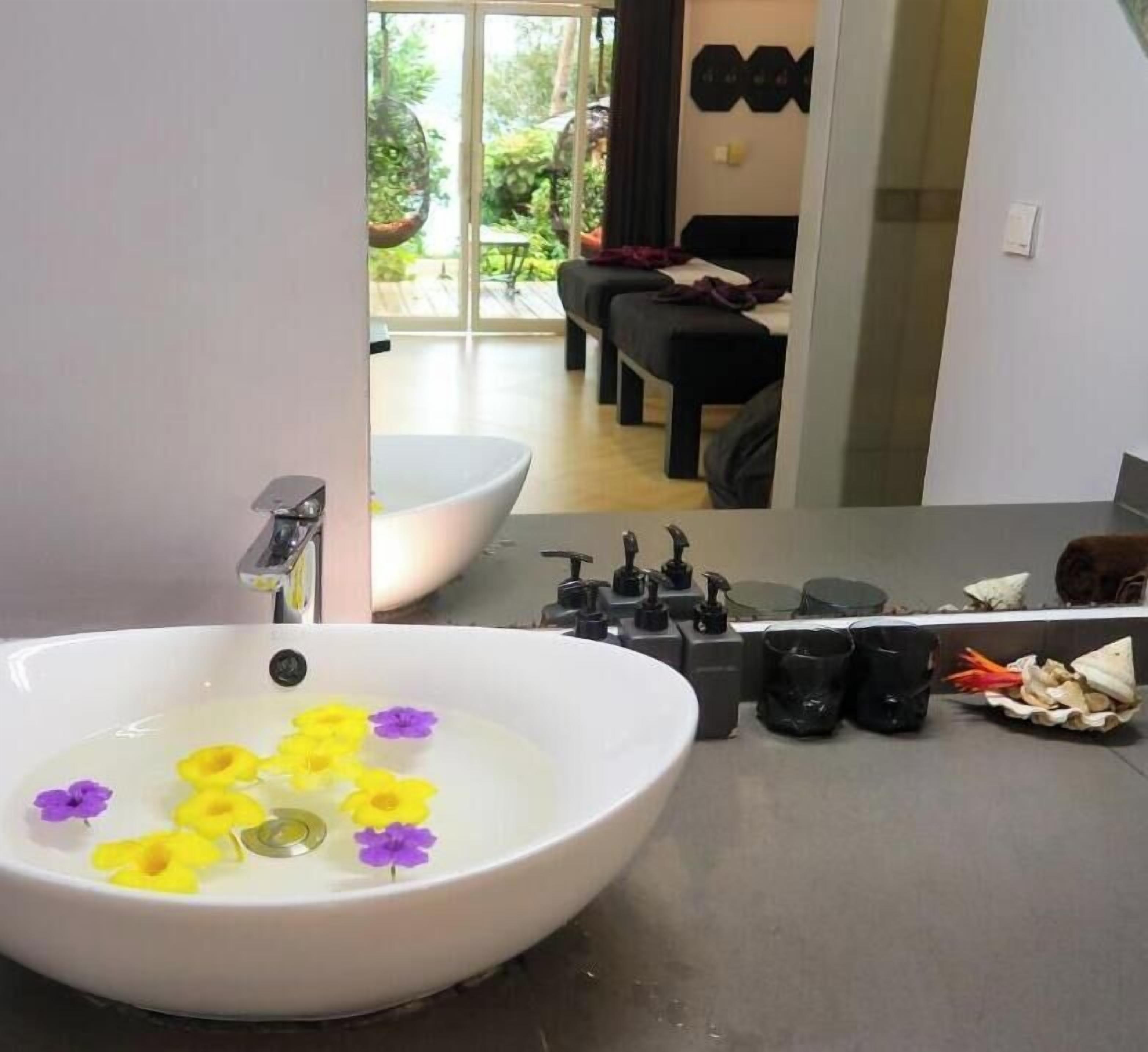 Uma casa de banho com uma grande pia branca, um espelho e vista para uma área de refeições com mesa e cadeiras.