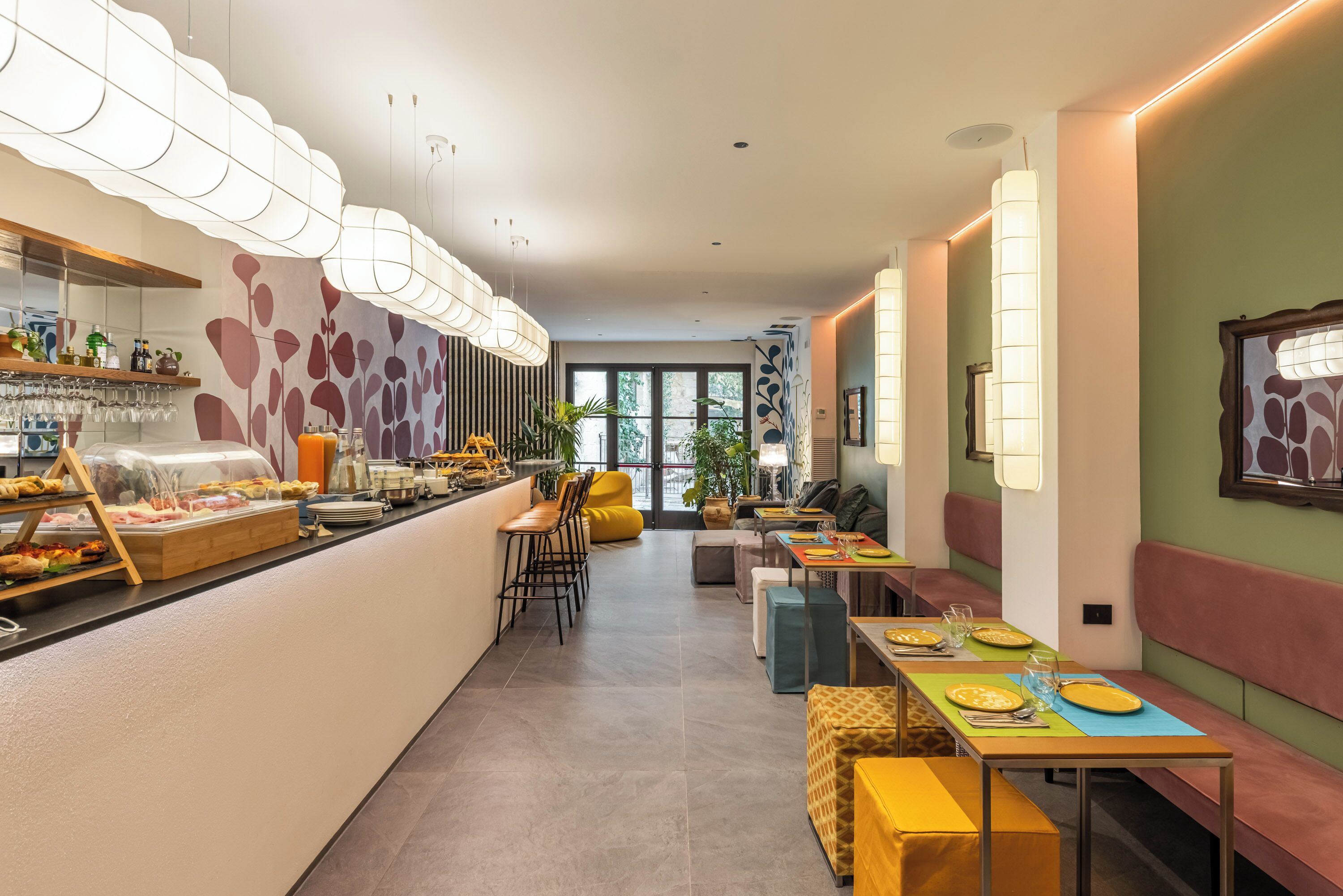 Uma área de refeições moderna com buffet à esquerda, disposição de mesas e vista para o exterior.