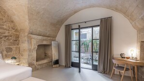 Um quarto acolhedor com parede de pedra, lareira, cama, escrivaninha com cadeira e vista para o exterior.