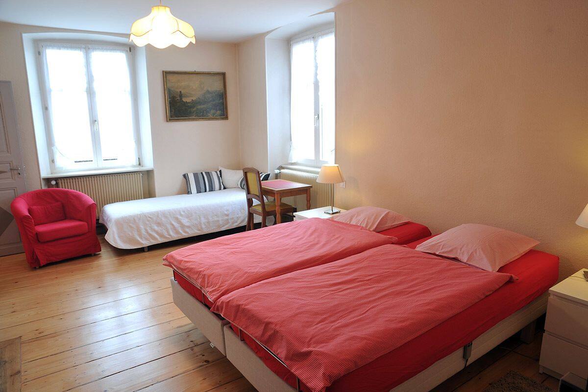 Quarto com duas camas, uma cadeira, uma mesa e um abajur.