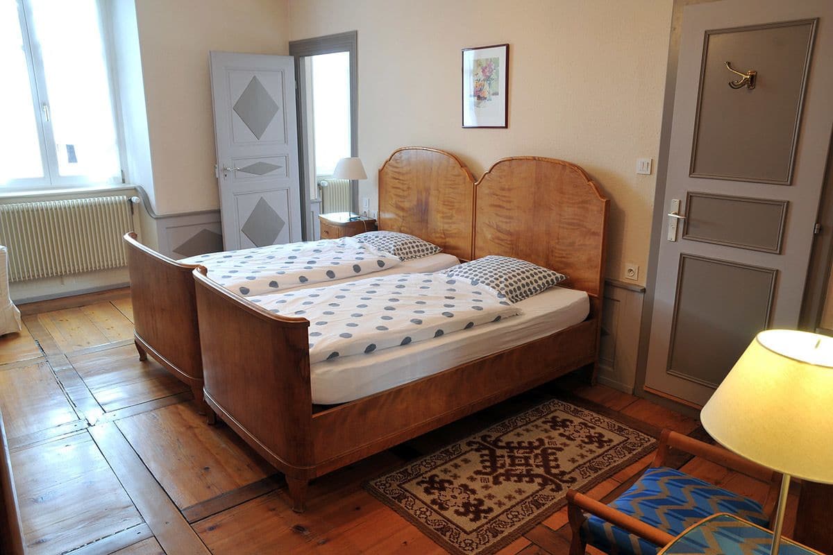 Um quarto com cama de madeira, mesa de cabeceira, luminária, porta e janela.