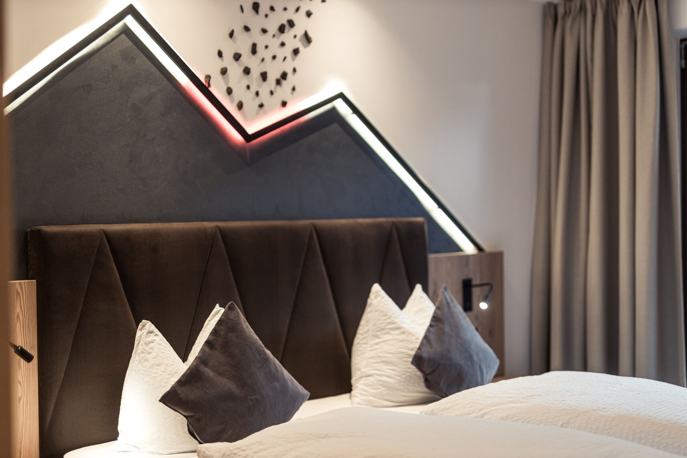 Quarto moderno com uma cama grande, cabeceira com design luminoso geométrico e luminária fixada na parede.
