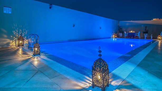 Piscina com deck revestido, rodeada por lanternas e uma mesa com cadeiras.