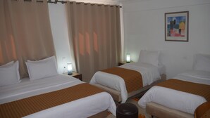 Quarto de hotel com duas camas, uma mesa de cabeceira com abajur, um quadro na parede e uma janela com cortinas.