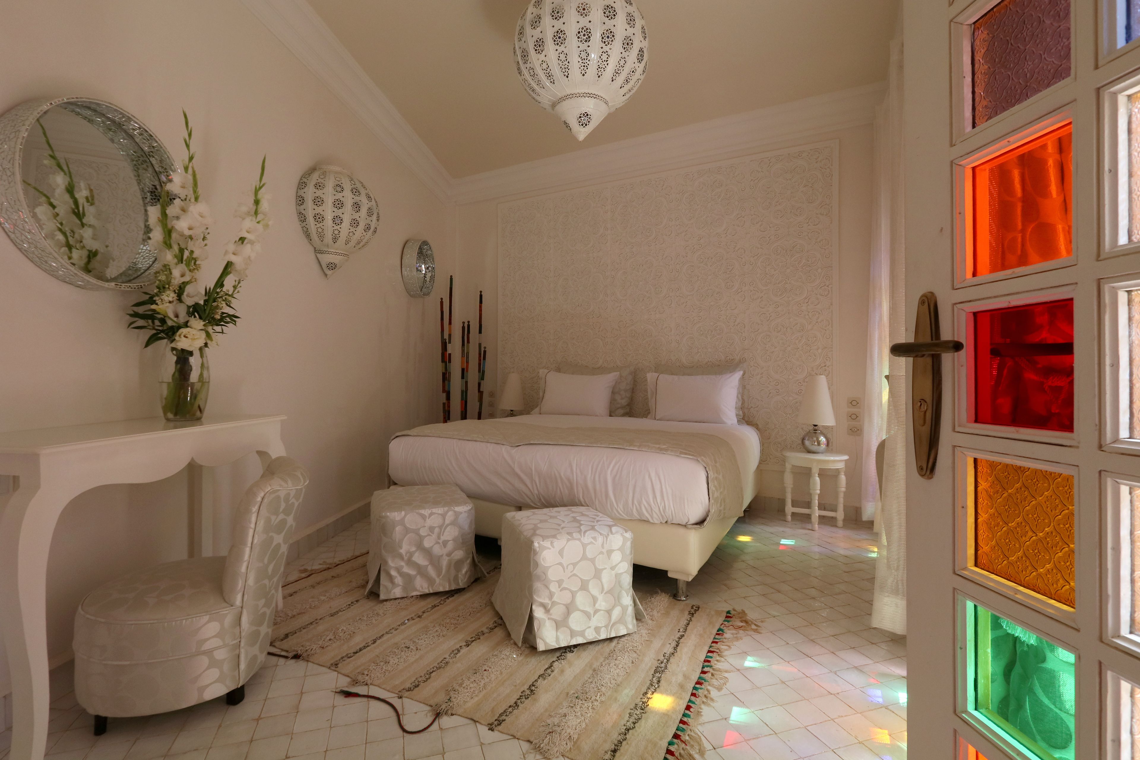 Quarto com cama, mesas de cabeceira, uma cadeira e um espelho decorativo.