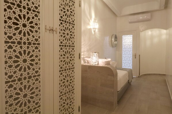 Quarto com cama, mesa de cabeceira, luminária na parede e porta de tela decorativa.