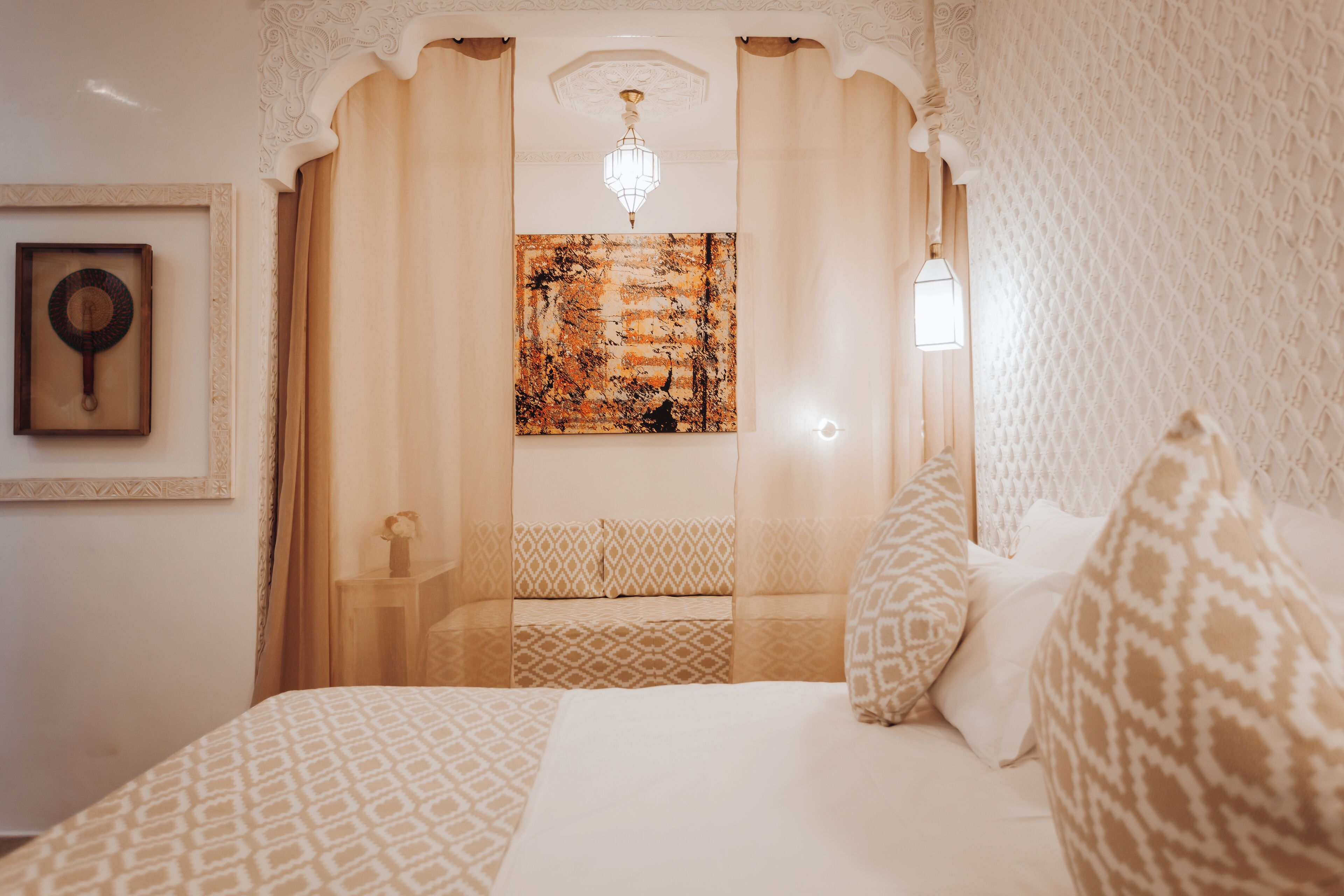 Quarto com cama, almofadas estampadas, obra de arte na parede e luminária decorativa no teto.