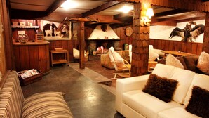 Um quarto aconchegante revestido em madeira, com lareira, um sofá branco e um espaço de bar.