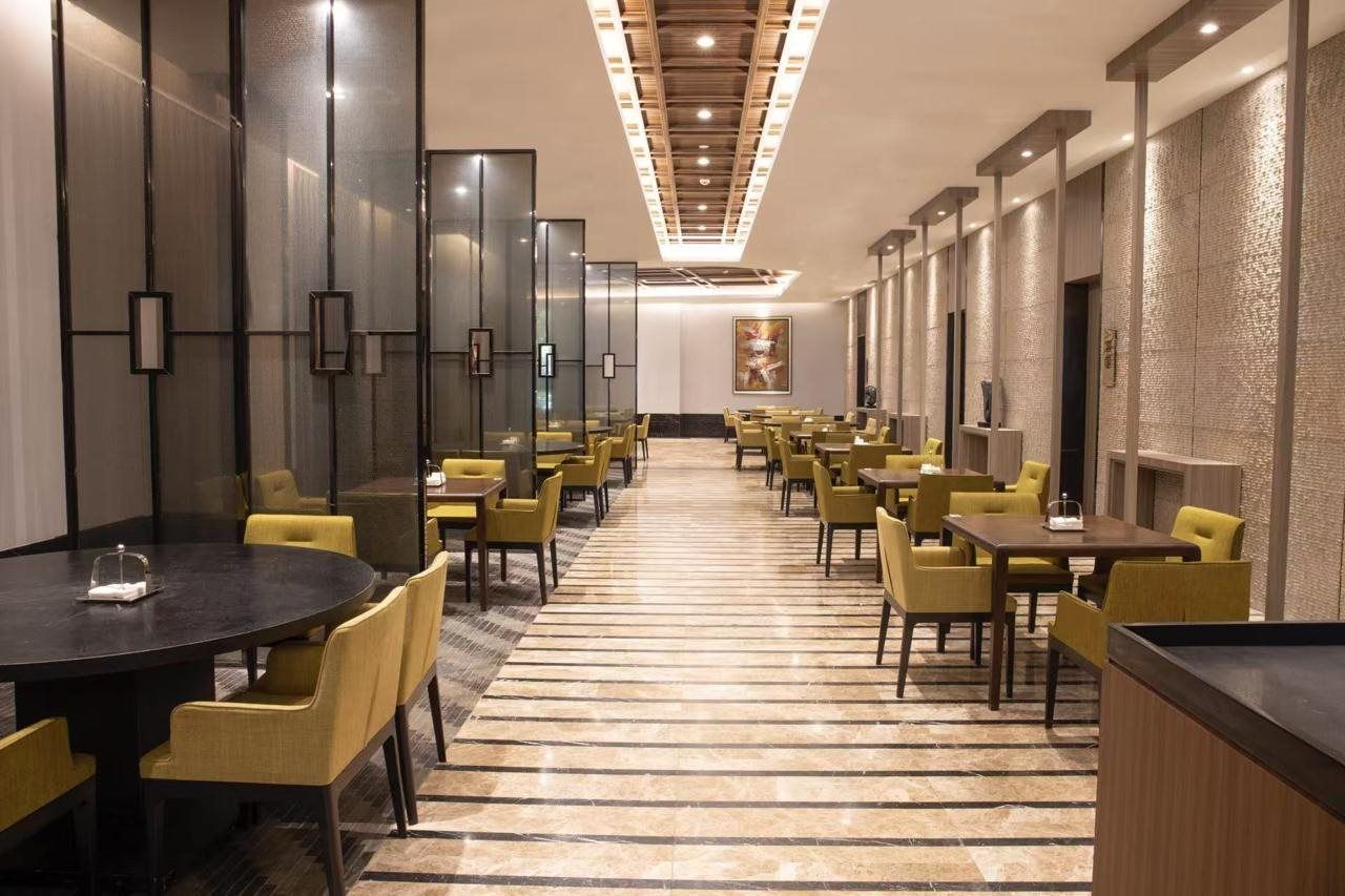 Um hall de hotel com um corredor comprido, várias áreas de estar e uma grande obra de arte na parede.