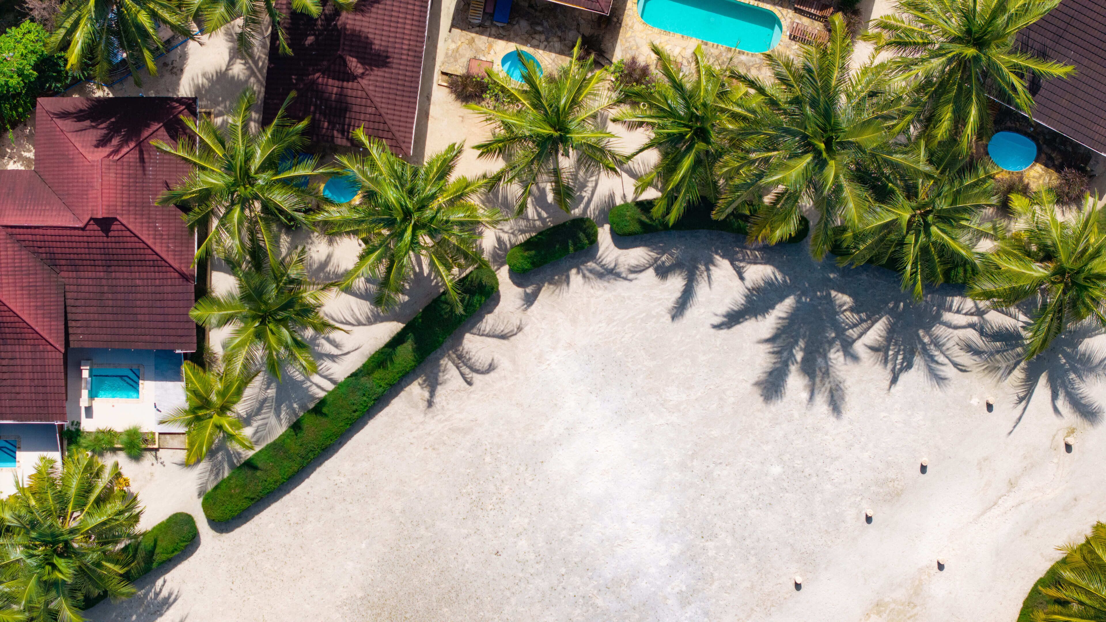 Vista aérea de um resort com várias piscinas, palmeiras e uma área de praia arenosa.
