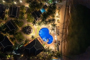 Vista aérea de um resort com piscina central, várias vilas para hóspedes e área de praia.