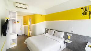 Quarto de hotel com cama, guarda-roupa, mesa de cabeceira e parede com frase motivacional.