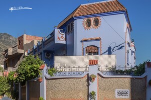 Um edifício de dois andares com fachada azul, telhado em telhas e uma varanda.