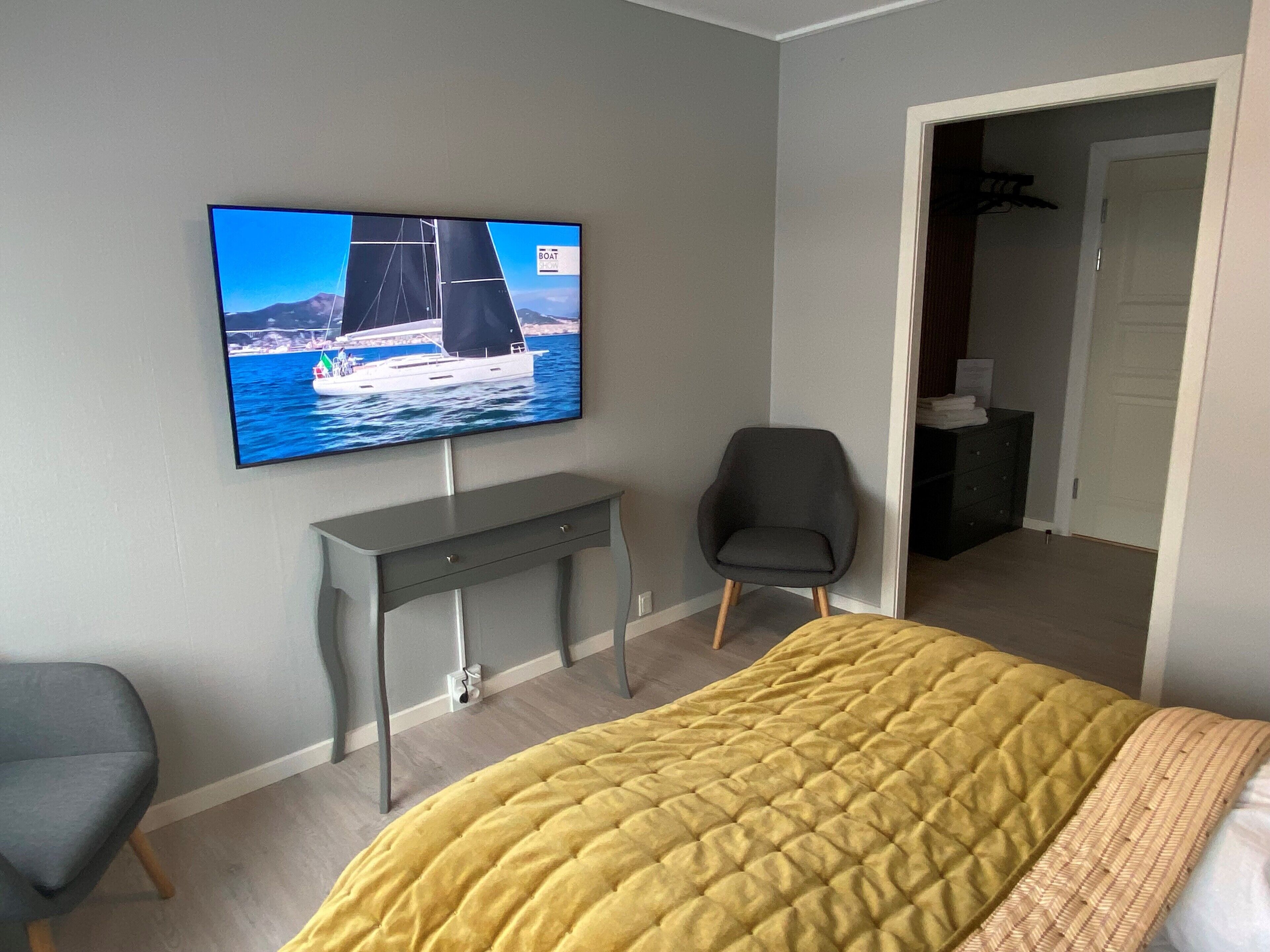 Quarto com cama, televisão na parede, escrivaninha e cadeira.
