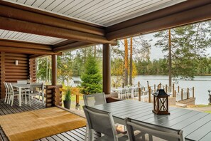 Um deck de madeira com mesa e cadeiras, com vista para um lago cercado por árvores e um píer.