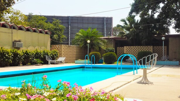 Uma piscina com um elemento aquático azul, rodeada por um muro baixo e um canteiro de flores com flores cor-de-rosa e brancas.