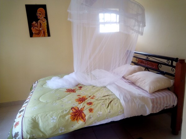 Uma cama com colcha florida, almofadas brancas e mosquiteiro.