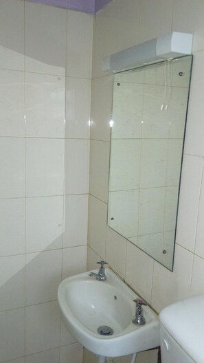 Casa de banho com azulejos brancos, uma pia com torneira e um espelho.