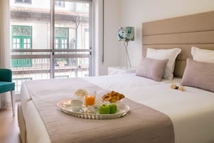 Cama bem arrumada com uma bandeja de itens de café da manhã, mesa de cabeceira e vista para uma varanda com grades verdes.