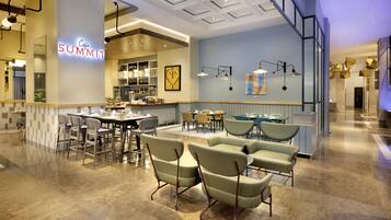 Um saguão de hotel moderno com área de bar, assentos e um letreiro chamativo que diz 'Cafe Summit'.